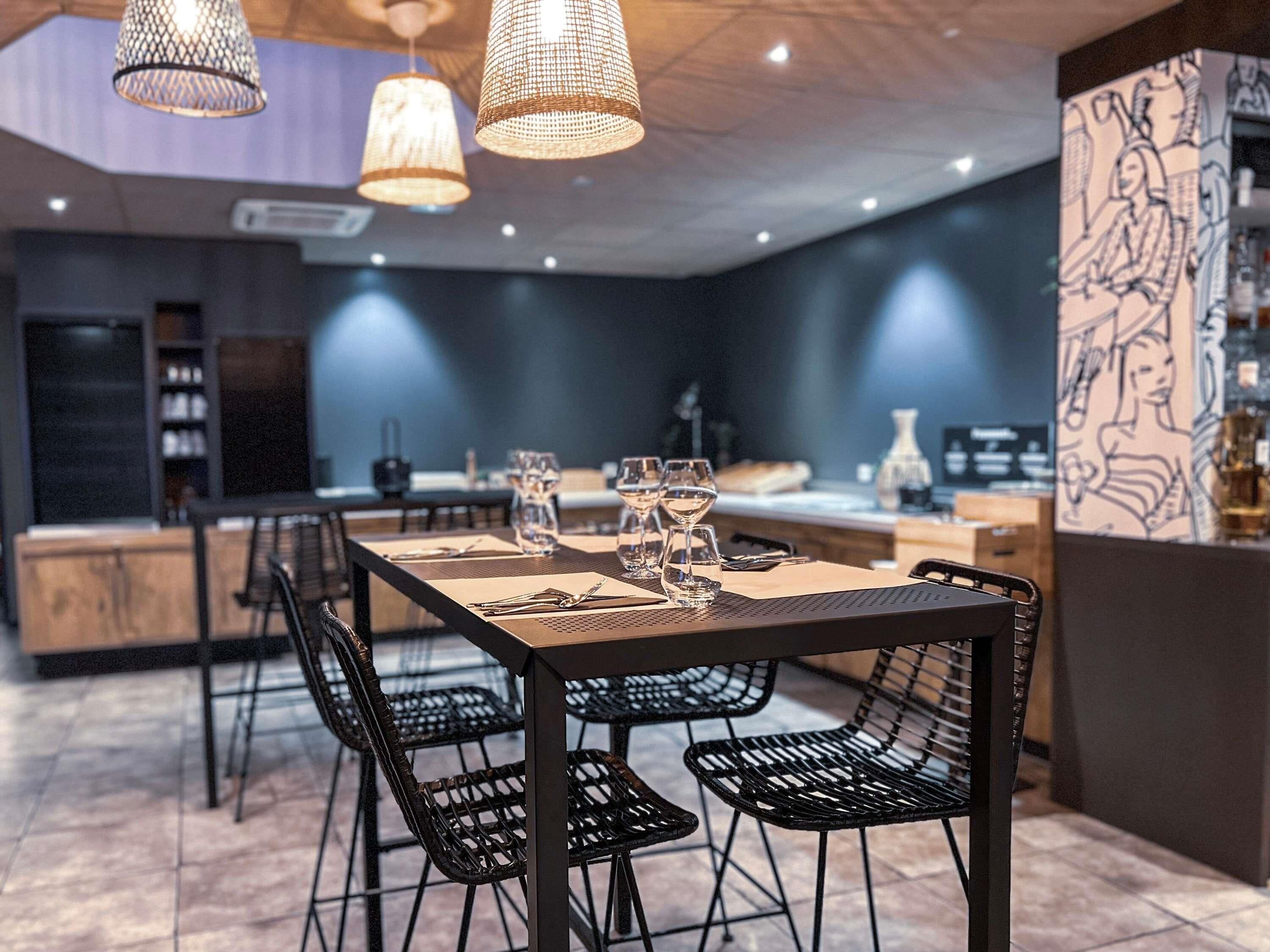 Uma sala de jantar moderna com uma mesa comprida, cadeiras pretas e luminárias pendentes.