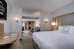 Quarto de hotel com uma cama grande, uma escrivaninha com cadeira, um sofá e uma TV fixada na parede.