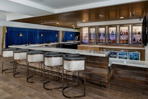 Uma área de bar moderna com um balcão comprido, vários bancos e um refrigerador de bebidas.