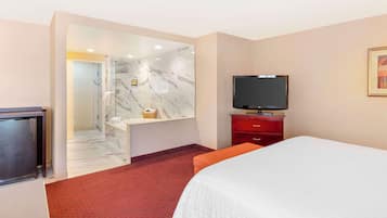 Quarto de hotel com cama, televisão, secretária com cadeira e casa de banho com chuveiro e sanita.