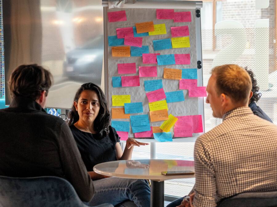 Sala de reuniões com parede de vidro, quadro branco com post-its e cadeiras modernas.
