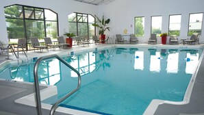 Piscina interna com água cristalina, rodeada por espreguiçadeiras e plantas em vasos.