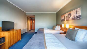 Quarto de hotel com duas camas, uma televisão, um quadro na parede e um corredor que dá para outro quarto.