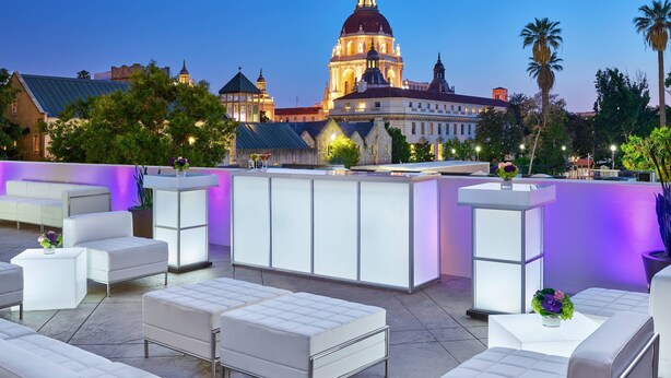 Um lounge no terraço com mobiliário branco e vista para um edifício histórico com cúpula.
