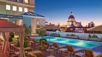 Área de piscina no terraço com espreguiçadeiras e guarda-sóis, vista de um edifício histórico com cúpula e aviso de segurança à beira da piscina.