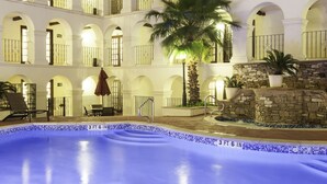 Um hotel com vários andares, piscina, varandas e uma parede de pedra.