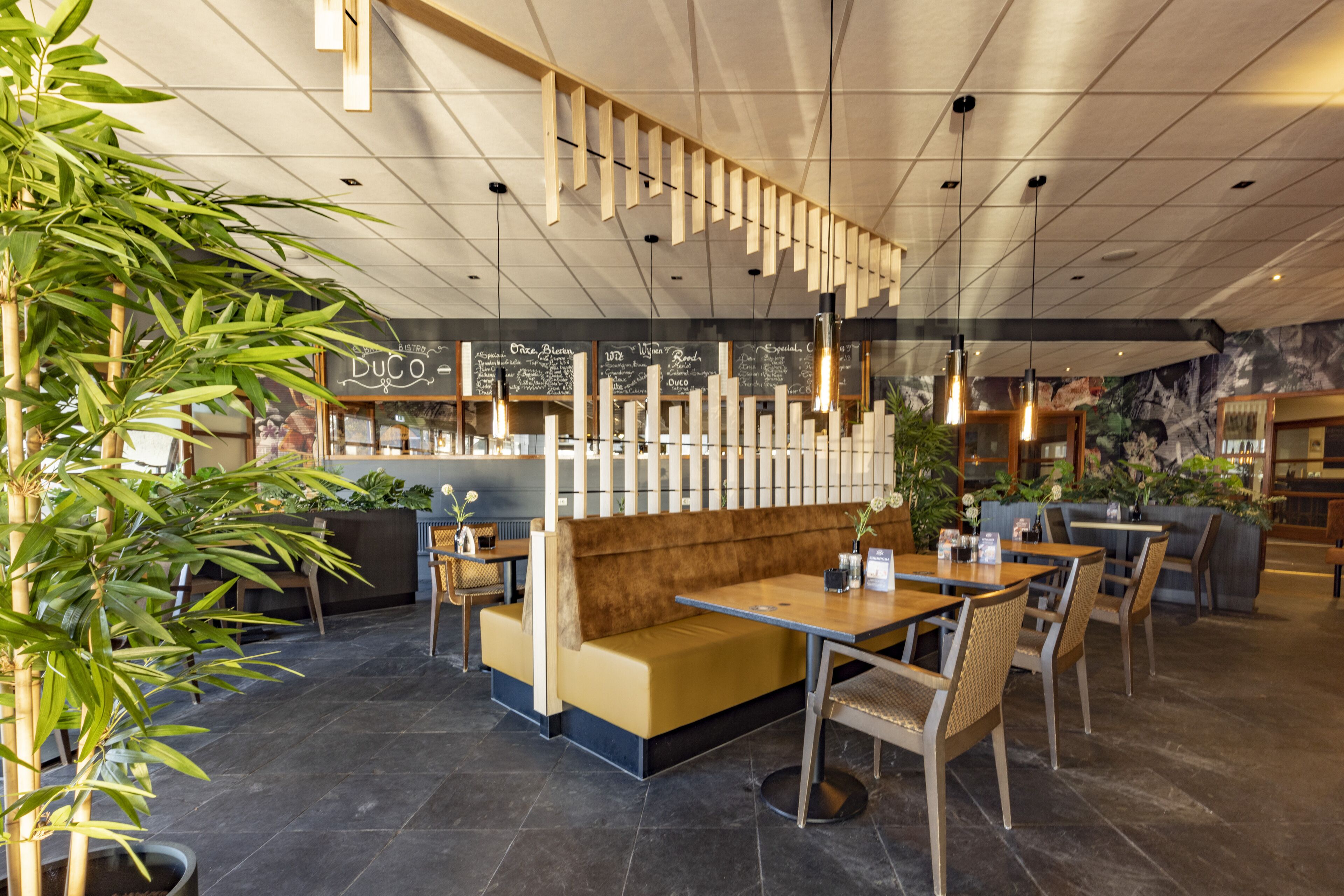 Interior de restaurante moderno com área de estar central, detalhes em madeira e plantas em vasos.
