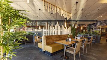 Interior de restaurante moderno com área de estar central, detalhes em madeira e plantas em vasos.