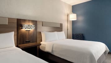 Quarto de hotel com duas camas, uma cabeceira de madeira, luminária fixada na parede e uma parede com detalhes em azul.