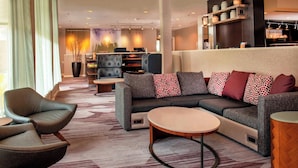 Um hall de hotel moderno com um sofá de canto, poltronas, uma mesa de centro e uma lareira.