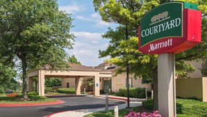 Entrada do hotel Courtyard Marriott com área de estacionamento coberta e jardim ajardinado com flores cor-de-rosa.