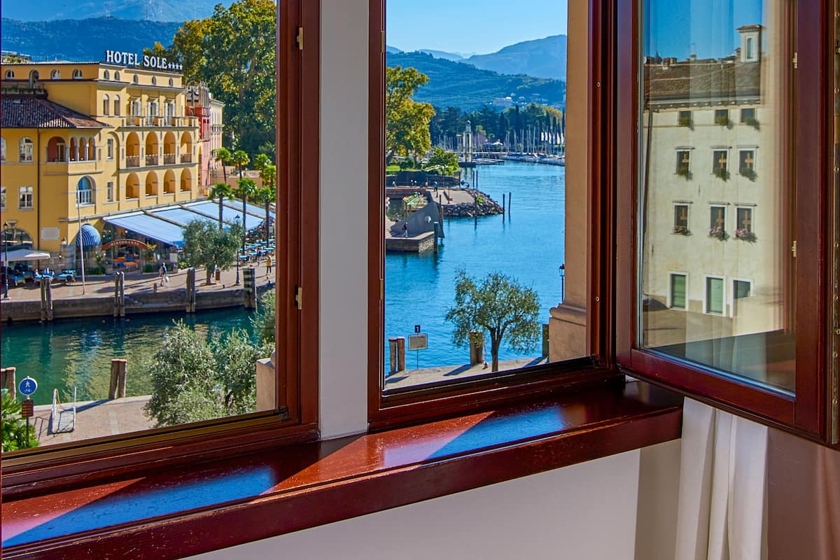 Quarto de hotel com uma grande janela em arco com vista para um corpo de água, um cais e uma cordilheira.
