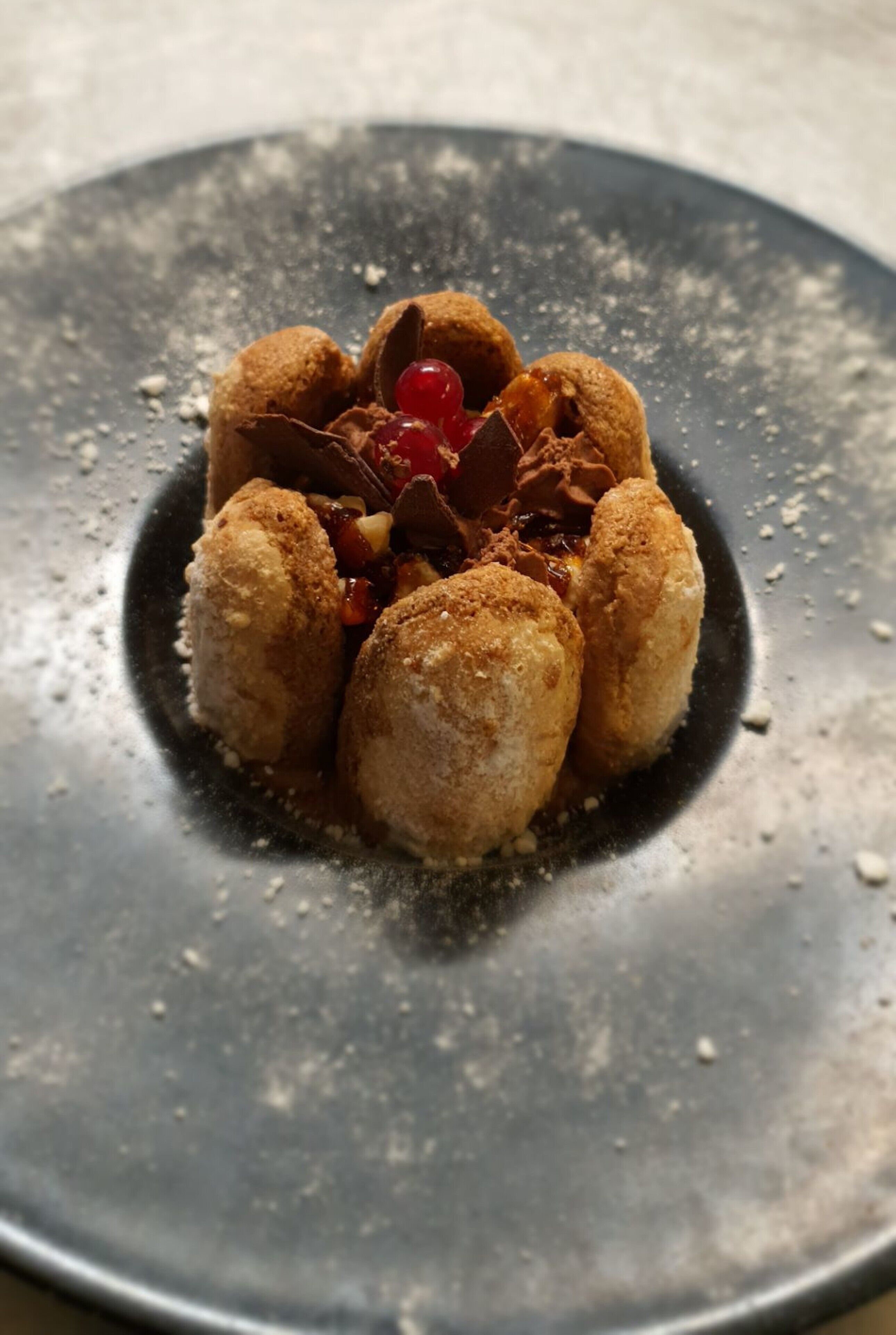 Uma sobremesa em um prato escuro, polvilhada com açúcar em pó.