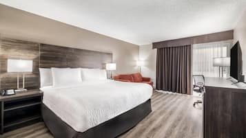 Quarto de hotel com uma cama grande, abajures, uma escrivaninha com cadeira e uma televisão.
