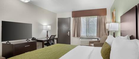 Quarto de hotel com cama, escrivaninha, cadeira, televisão e janela com cortinas.