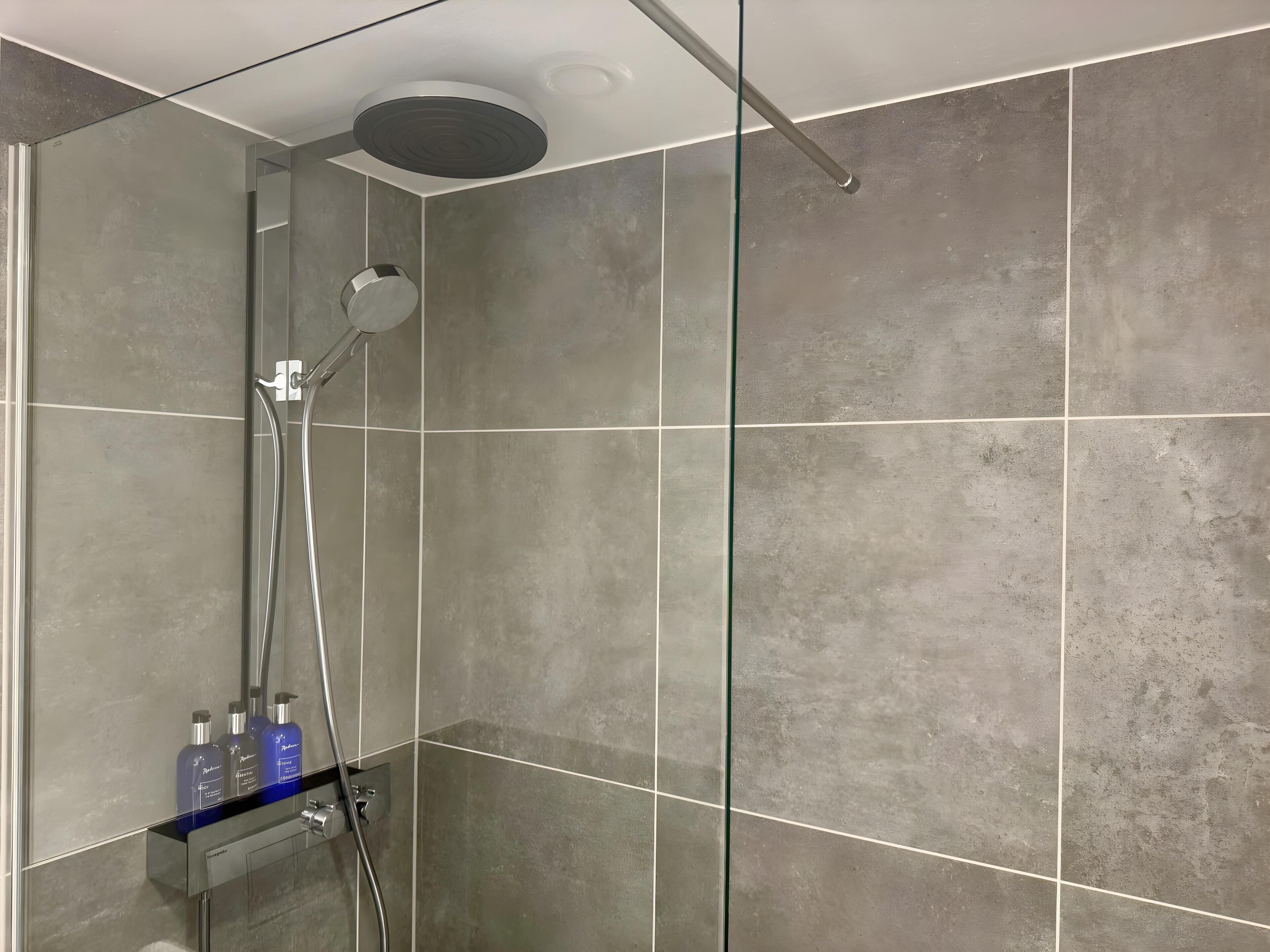 Um chuveiro moderno com divisória de vidro, azulejos cinzas e um chuveiro manual.