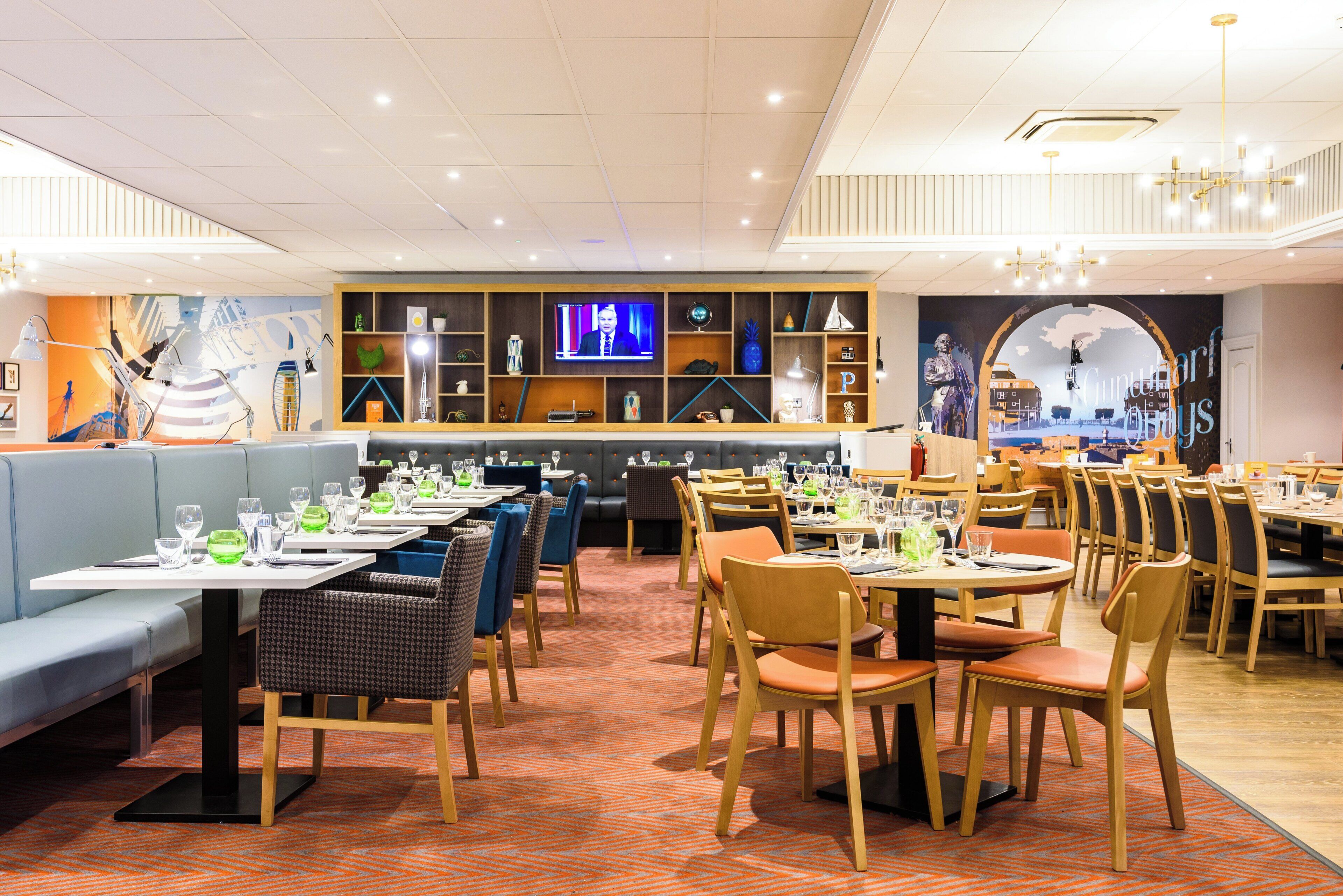 Um restaurante com várias áreas de refeição, incluindo cabines e mesas, e uma tela de televisão na parede.
