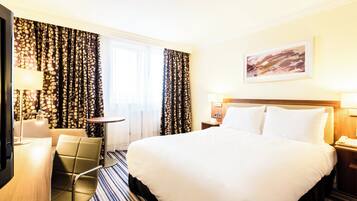 Quarto de hotel com uma cama, escrivaninha, cadeira, mesa e um quadro na parede.