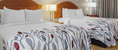Quarto de hotel com duas camas, cabeceiras de madeira, roupa de cama branca e uma janela grande com cortinas.