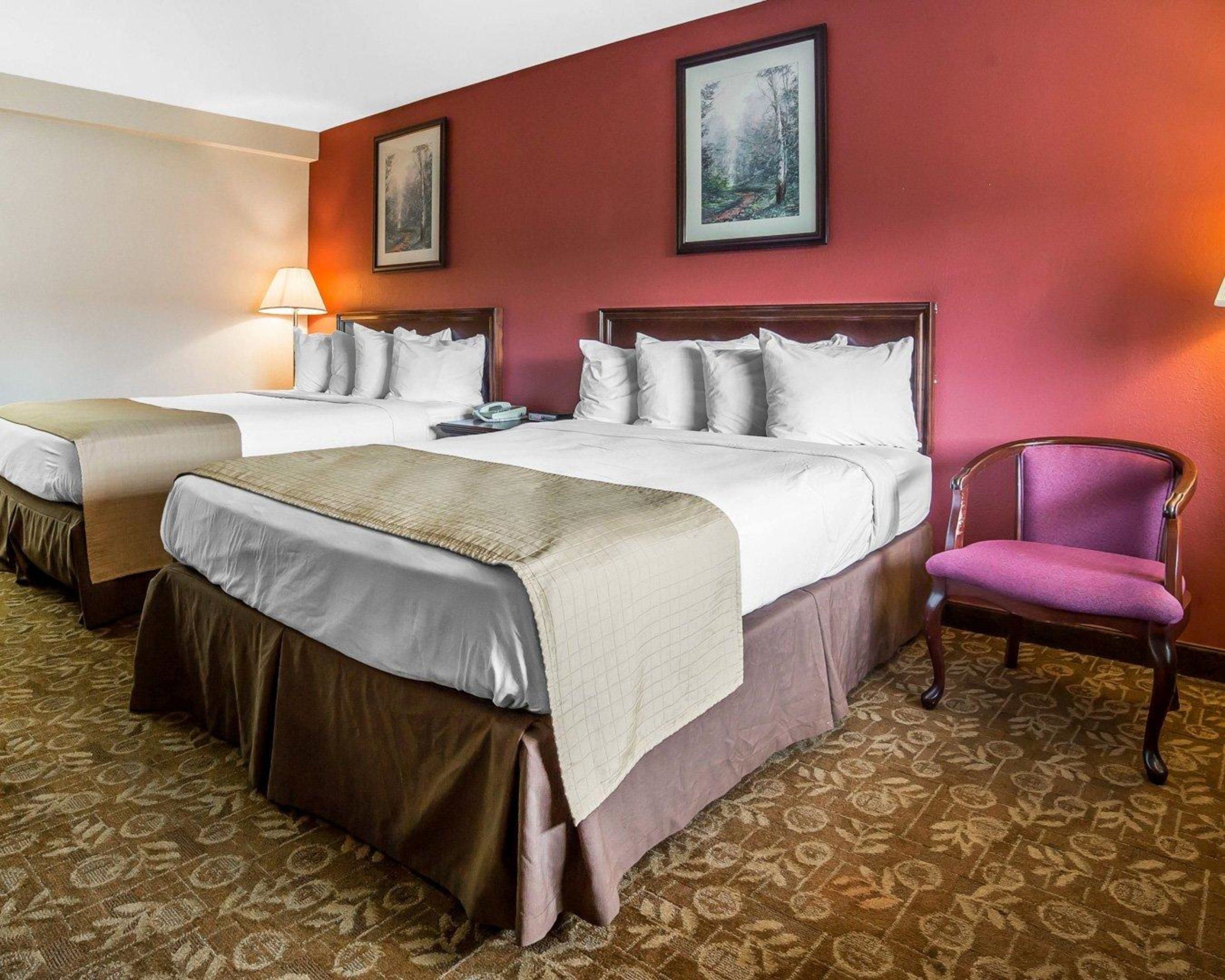 Quarto de hotel com duas camas, uma cadeira e um abajur.