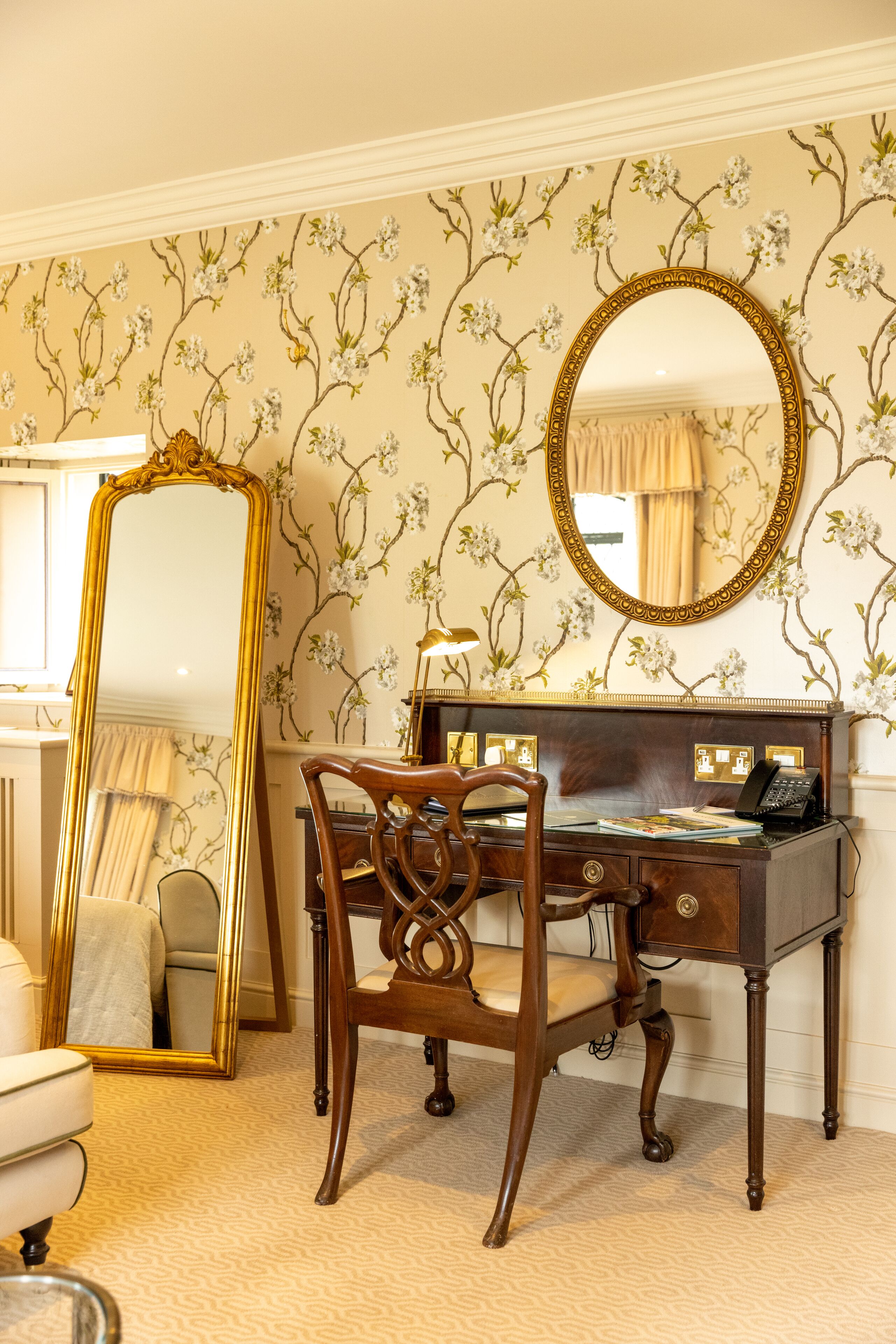 Quarto com escrivaninha de madeira, um espelho grande e uma cadeira.