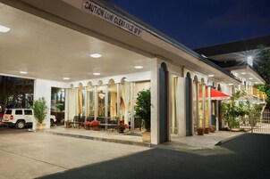 Entrada de hotel com placa de aviso, área de estar externa e plantas em vasos.
