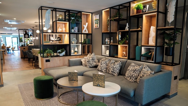 Uma sala de estar moderna com um sofá, duas mesas redondas e pufes verdes.