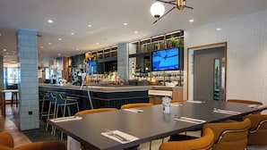 Uma área de bar moderna com um balcão comprido, banquetas e uma tela de televisão.