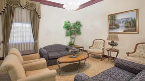 Uma sala de estar com uma janela grande, duas poltronas, um sofá, uma mesa de centro e um quadro na parede.