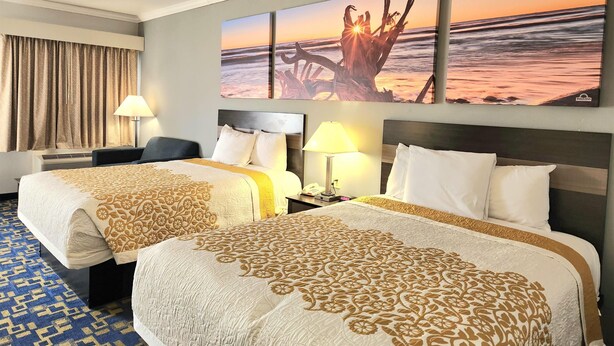 Quarto de hotel com duas camas, uma escrivaninha e vista para o oceano ao pôr do sol.