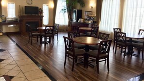 Uma sala de jantar espaçosa com mesas e cadeiras de madeira, uma lareira e uma grande janela com cortinas.