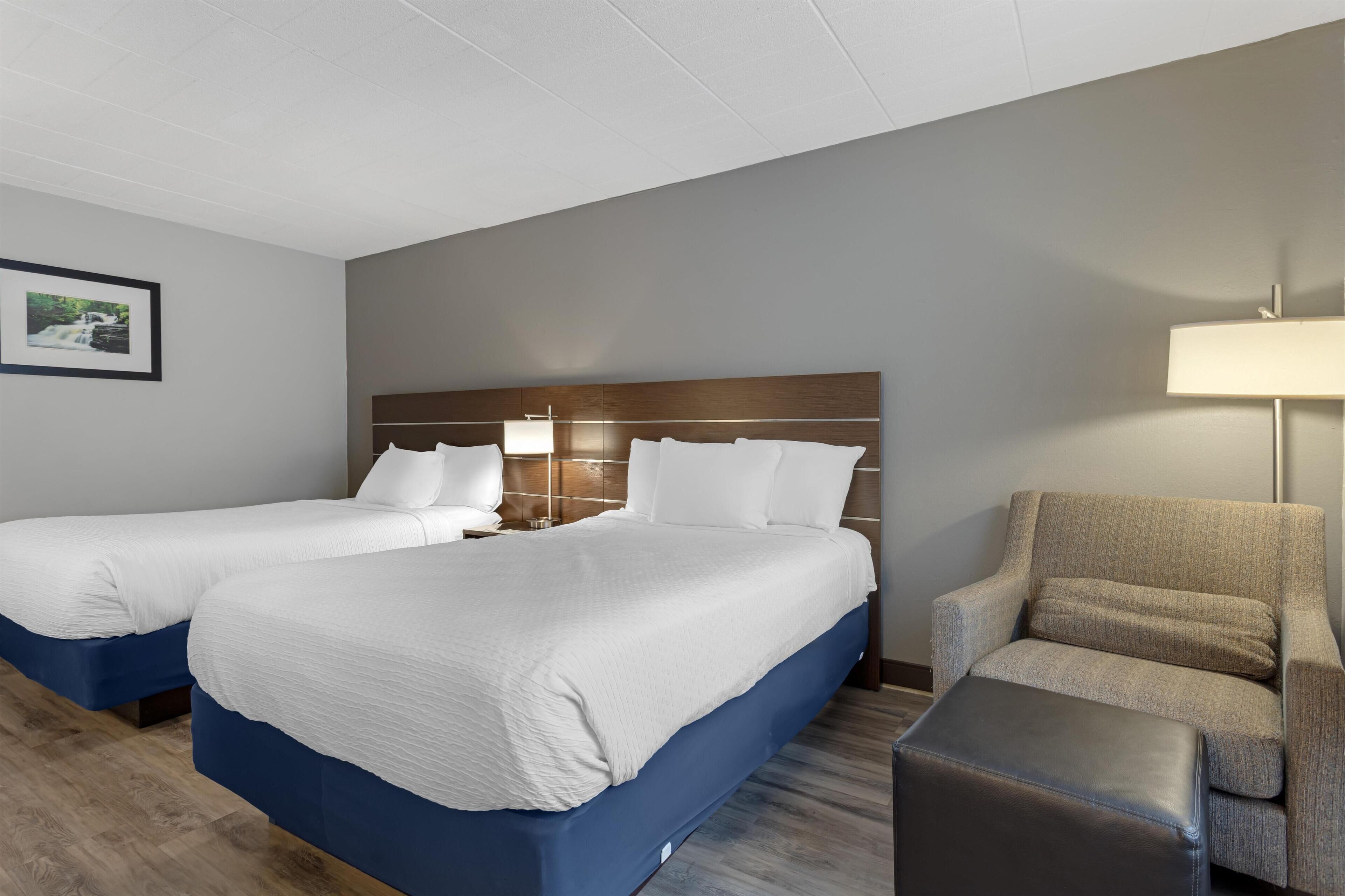 Quarto de hotel com duas camas, um sofá, uma luminária e um quadro na parede.