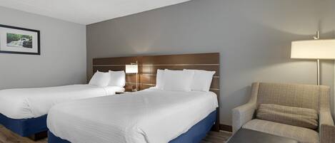 Quarto de hotel com duas camas, um sofá, uma luminária e um quadro na parede.