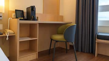 Quarto de hotel compacto com escrivaninha, cadeira e telefone.