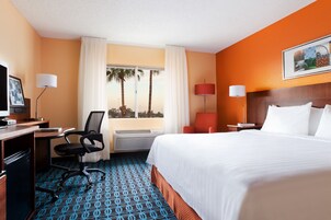 Quarto de hotel com cama, escrivaninha, cadeira e janela com cortinas.