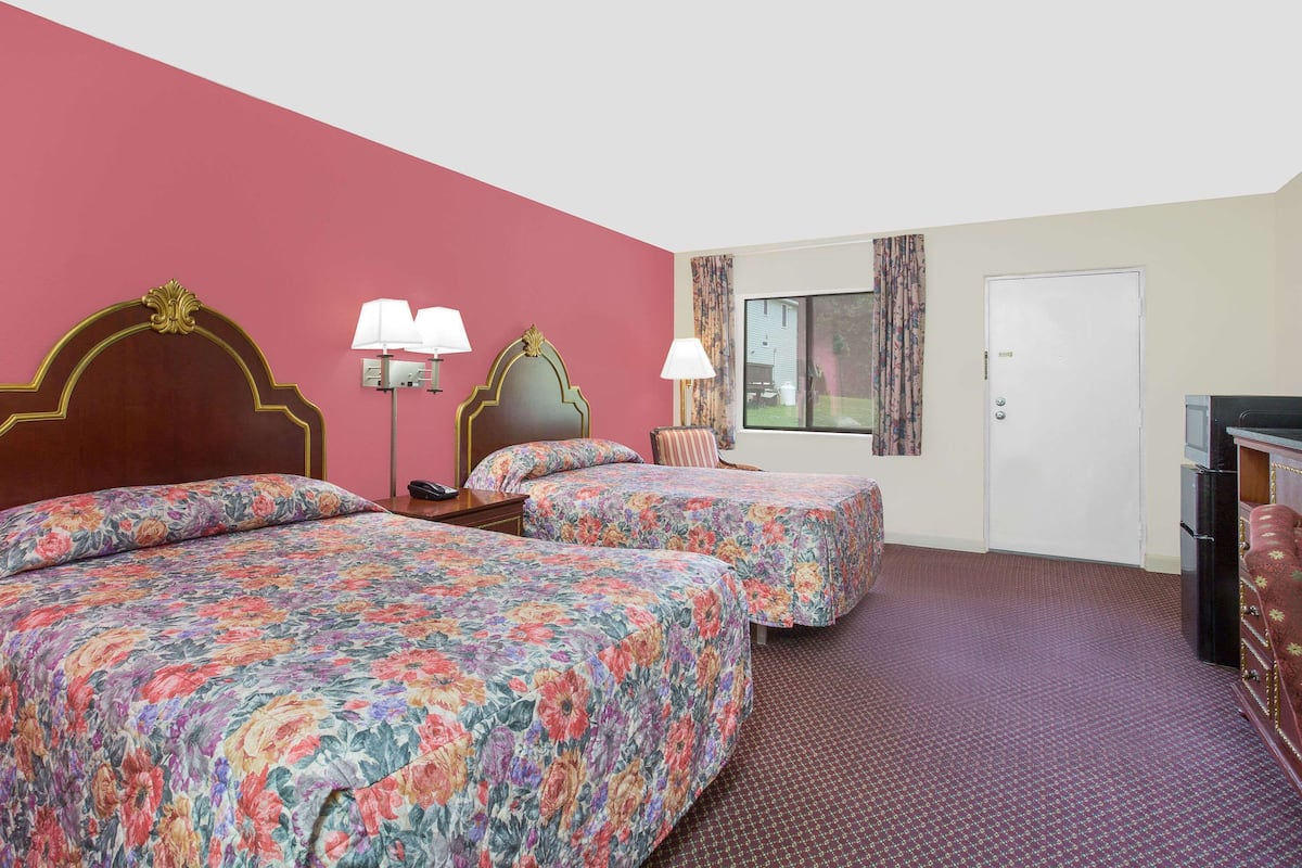 Quarto de hotel com duas camas, uma escrivaninha, uma cadeira, um abajur e uma televisão.
