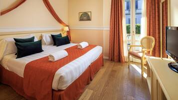 Quarto de hotel com uma cama grande, duas almofadas, televisão, cadeira e janela com cortinas.