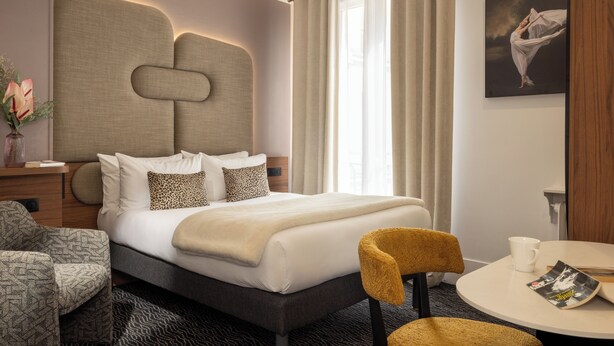 Quarto de hotel moderno com uma cama grande, uma mesa redonda, um sofá e um quadro na parede.