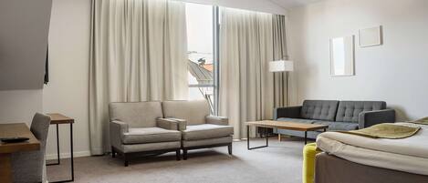 Quarto de hotel moderno com sofá, poltrona, mesa de jantar e cama.