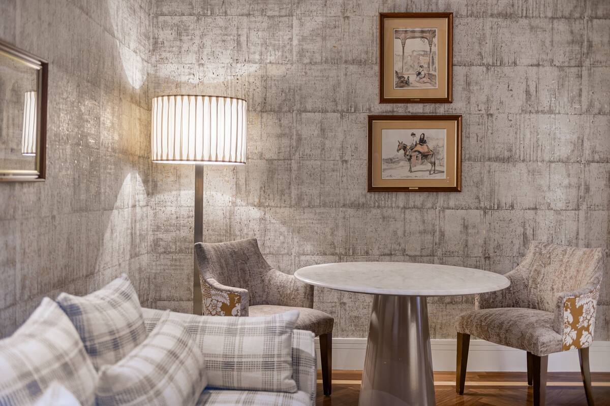 Um quarto com parede de concreto, uma mesa redonda, duas poltronas, um sofá e um abajur.