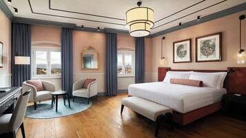 Quarto de hotel com uma cama grande, uma escrivaninha, uma cadeira, uma mesa redonda e vista para a cidade pela janela.