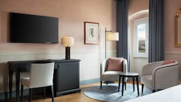 Quarto de hotel com televisão de ecrã plano, secretária com cadeira, sofá, mesa pequena e candeeiro.
