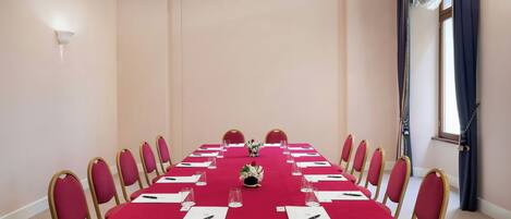 Uma sala de conferências com uma mesa comprida, cadeiras e um arranjo de flores.