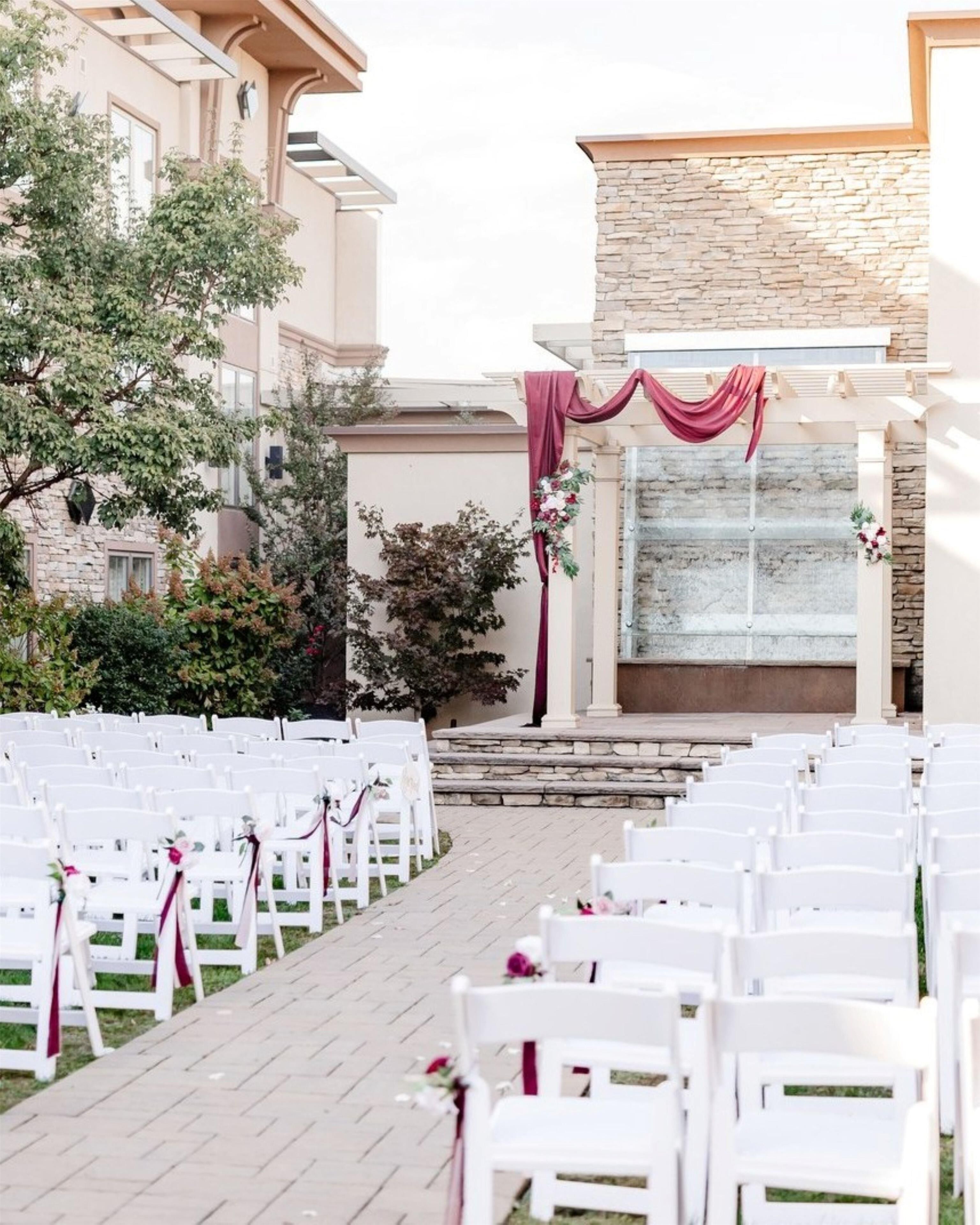 Um corredor de casamento com cadeiras brancas e um edifício de pedra ao fundo.