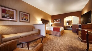 Quarto de hotel com sofá, cama, televisão, escrivaninha e banheiro visível por uma abertura em arco.