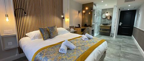 Quarto de hotel com cama grande, parede com ripas de madeira, banheiro com pia e espelho, e porta que dá para outro cômodo.
