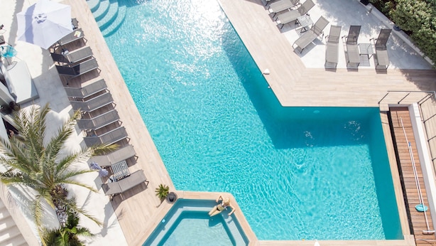 Uma piscina retangular grande com água azul cristalina, rodeada por espreguiçadeiras e guarda-sóis.