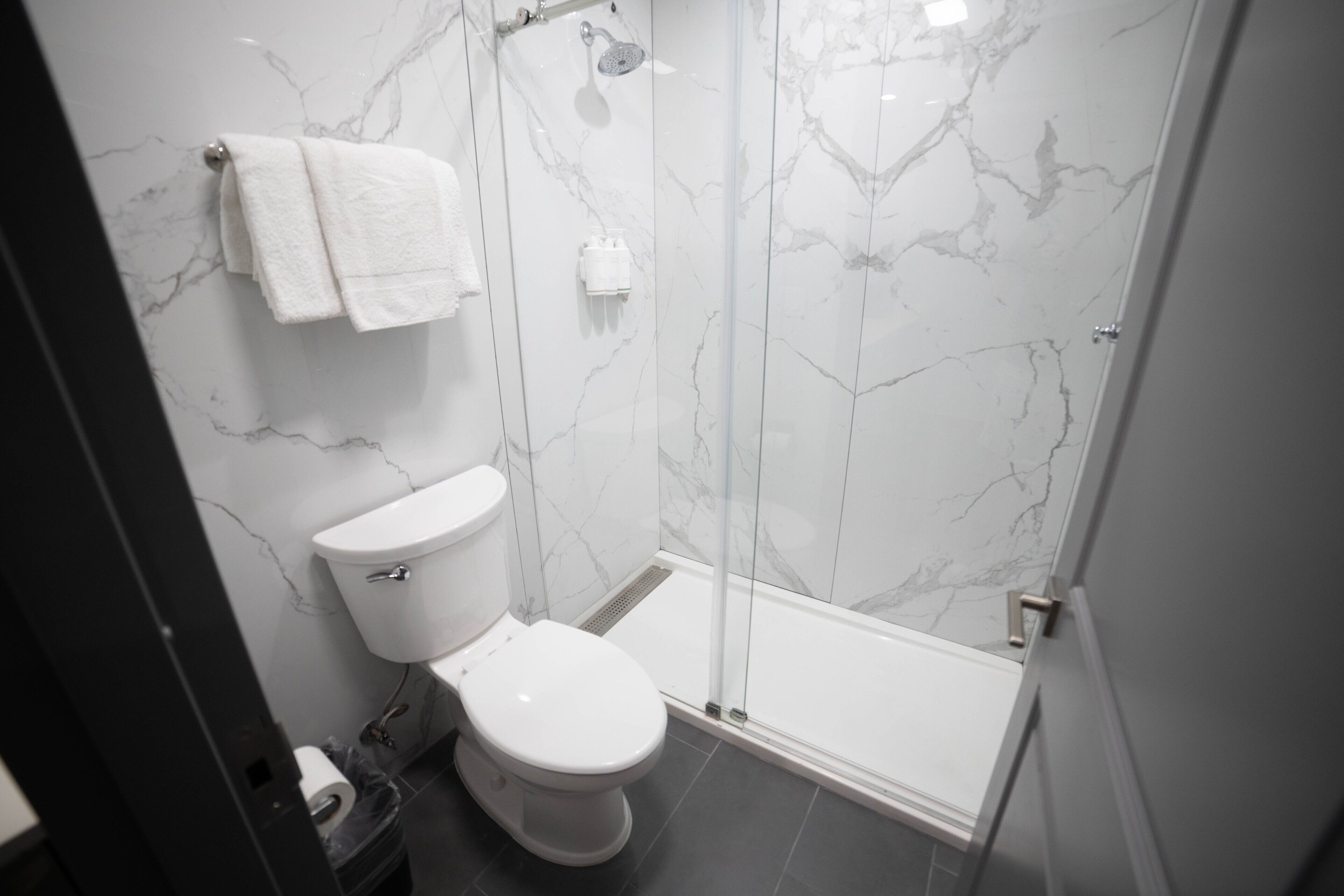 Um banheiro moderno com vaso sanitário, chuveiro em box de vidro e paredes de mármore.