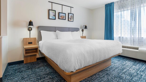 Quarto de hotel com uma cama grande, duas mesas de cabeceira, televisão presa à parede e uma janela com cortinas.