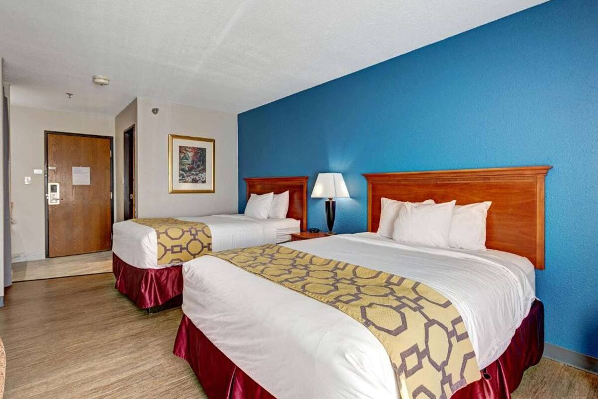 Quarto de hotel com duas camas, cabeceira de madeira, parede azul e um quadro na parede.